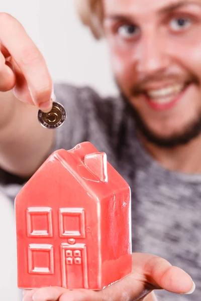 Man putting money into house piggybank - Stock Image - Everypixel