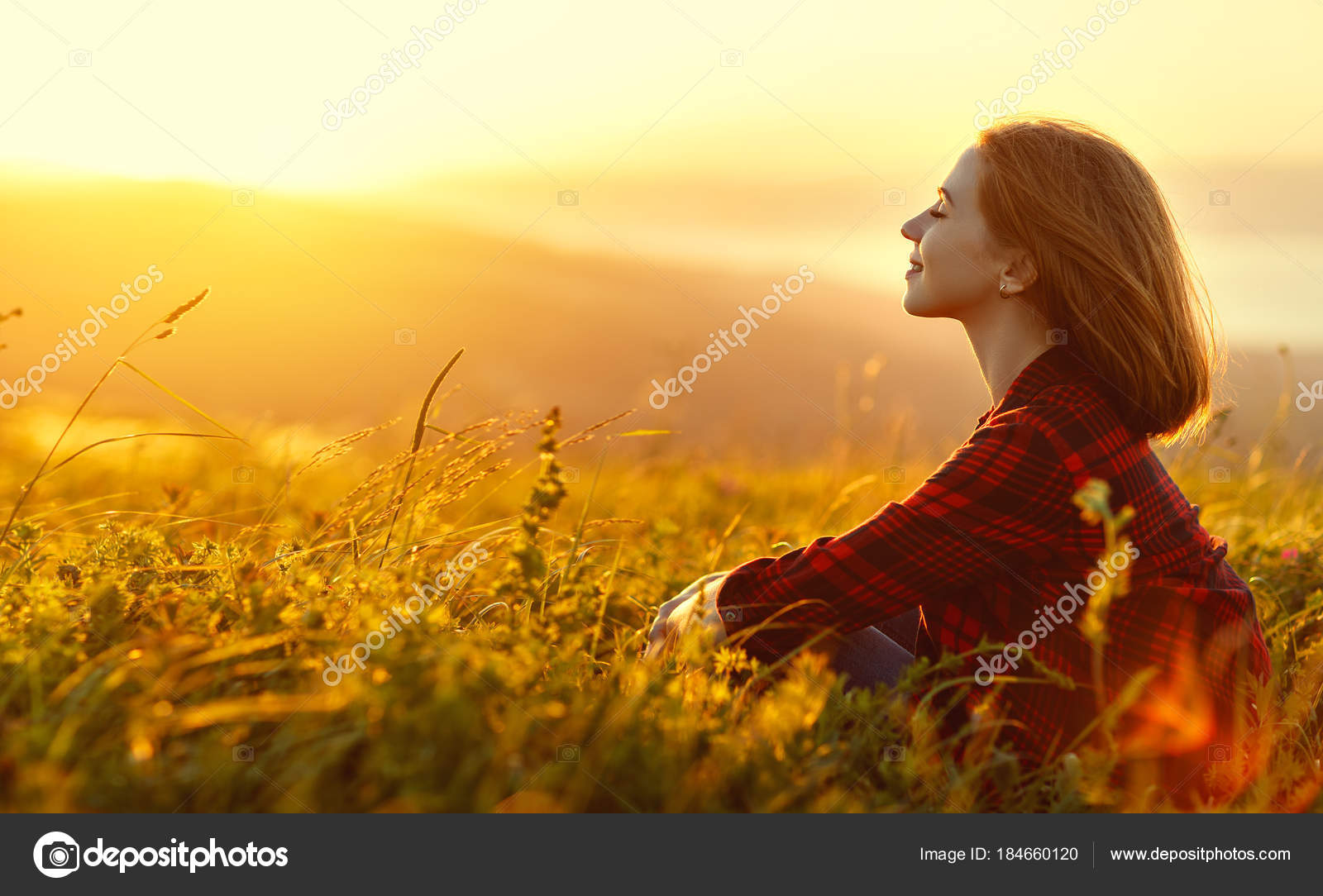Woman sits with her back in the field and look sunset in the mou ...