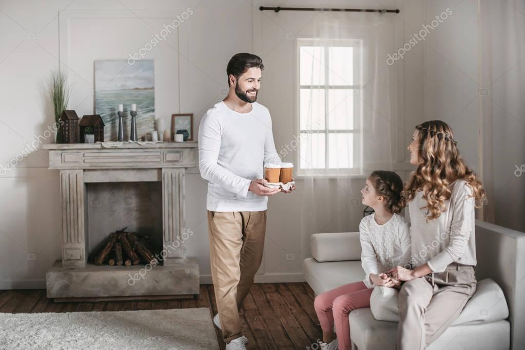 Sonriente padre trayendo café en vasos de papel para la madre y la hija ...