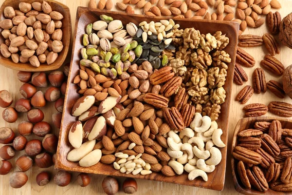 Six types of nuts in a round wooden form (almonds, hazelnuts, pine nuts ...