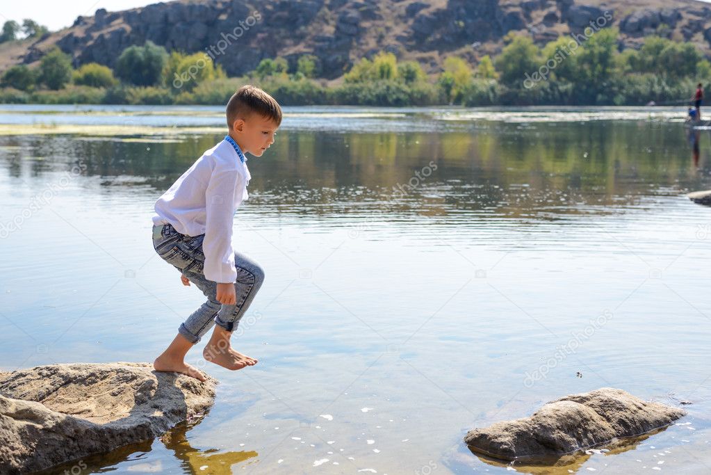 Niño pequeño jugando en las rocas en el lago 2023