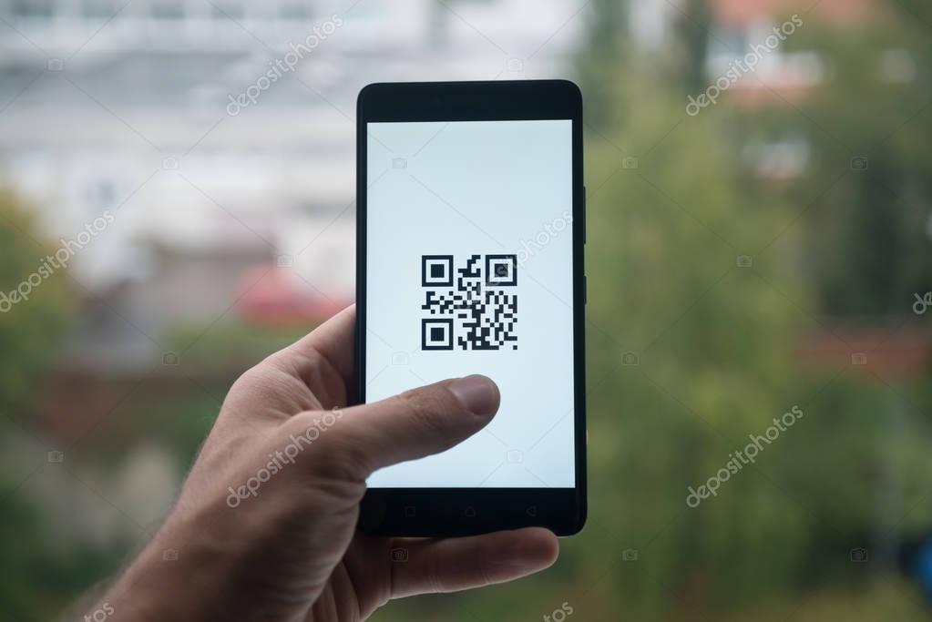 Hombre sosteniendo smartphone con código QR con el dedo en la pantalla ...