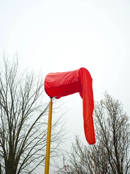 A bright red fabric wind sock on top of a yellow pole hangs limp along ...