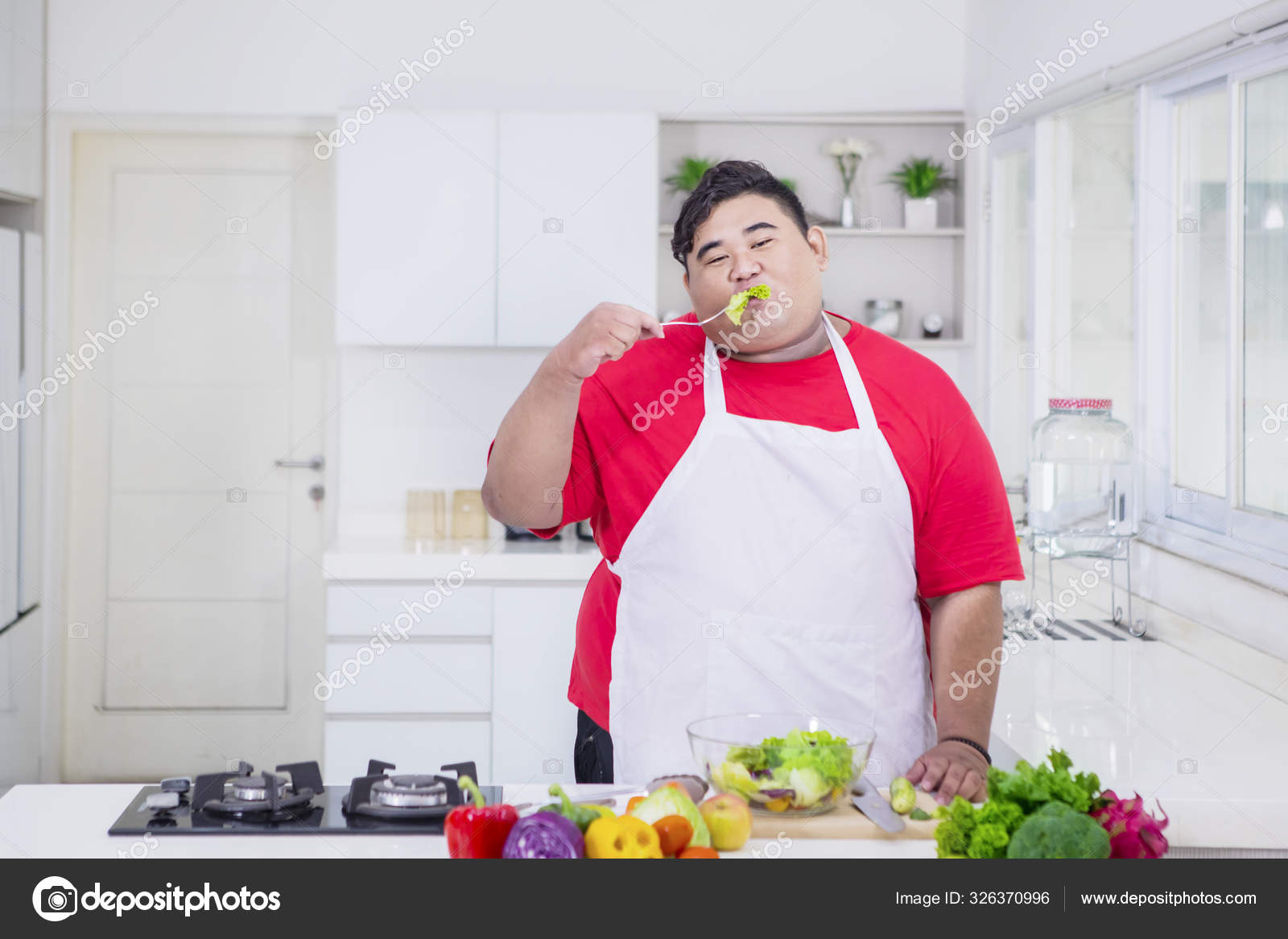 Fat Asian man biting a lettuce in the kitchen Stock Photo by ...
