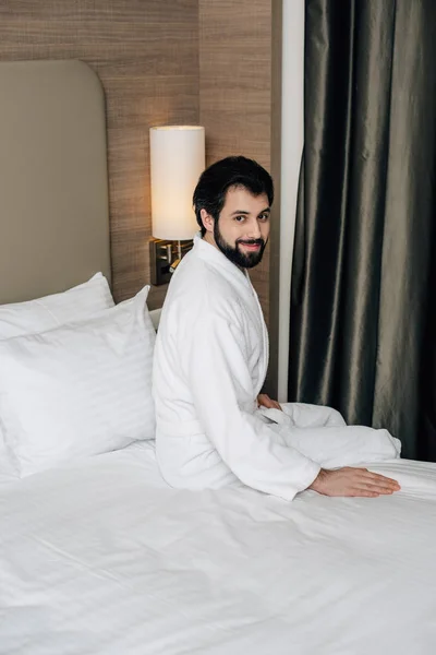 happy man in bathrobe sitting on bed at hotel suite - Stock Image ...