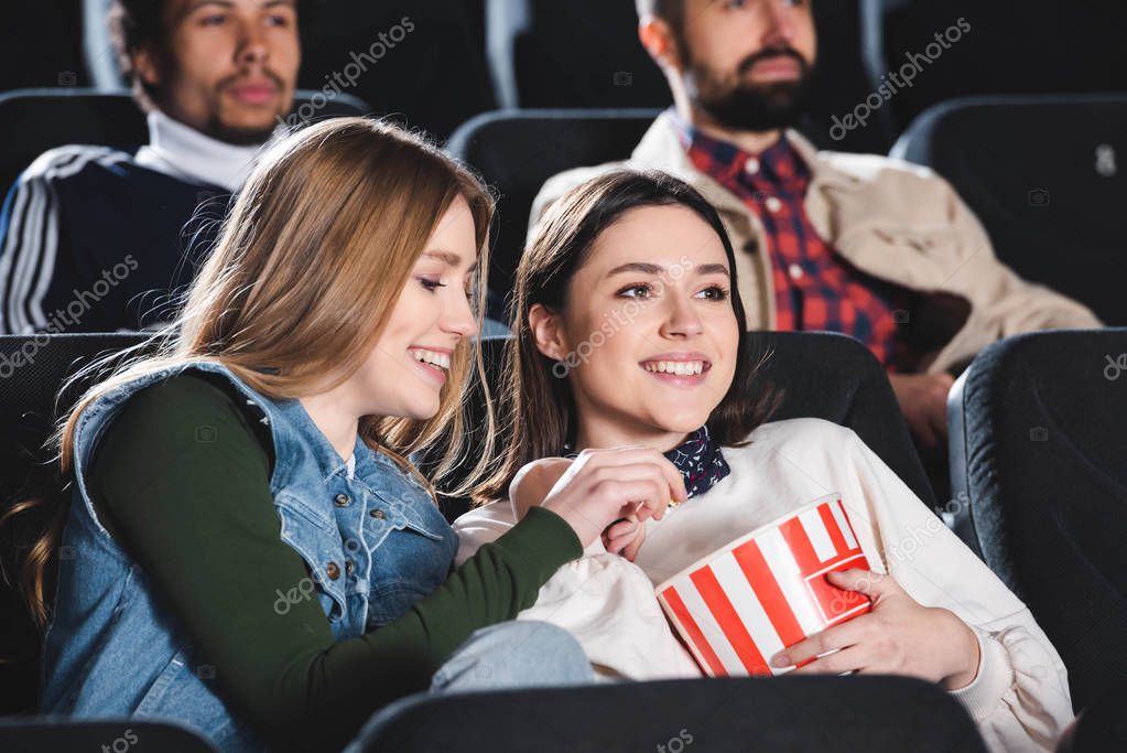 enfoque selectivo de amigos sonrientes con palomitas de maíz viendo ...