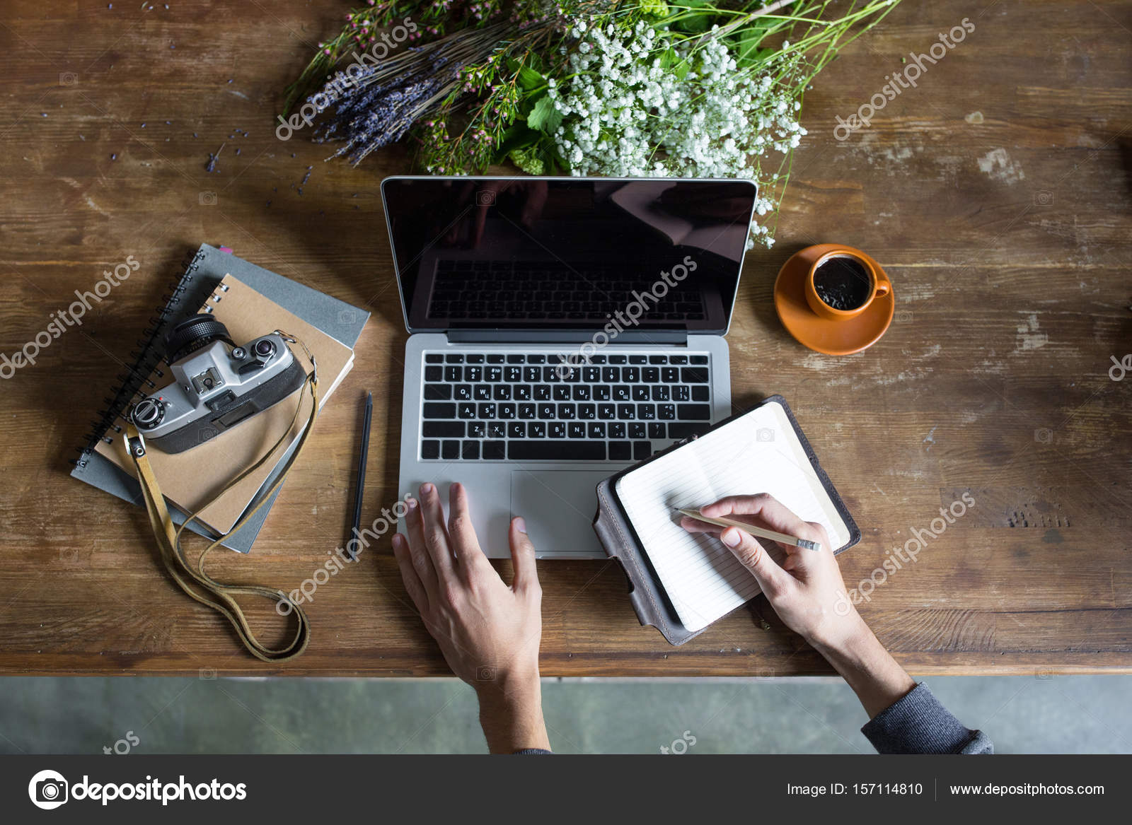 Person using laptop and graphic tablet at workspace with notebooks and ...