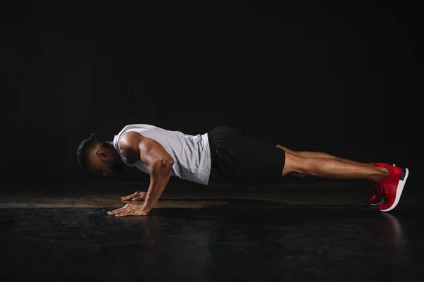 side view of young african american sportsman doing push-ups on black ...