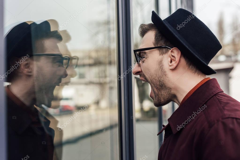 hombre enojado en sombrero gritando en su reflejo en la ventana 2023