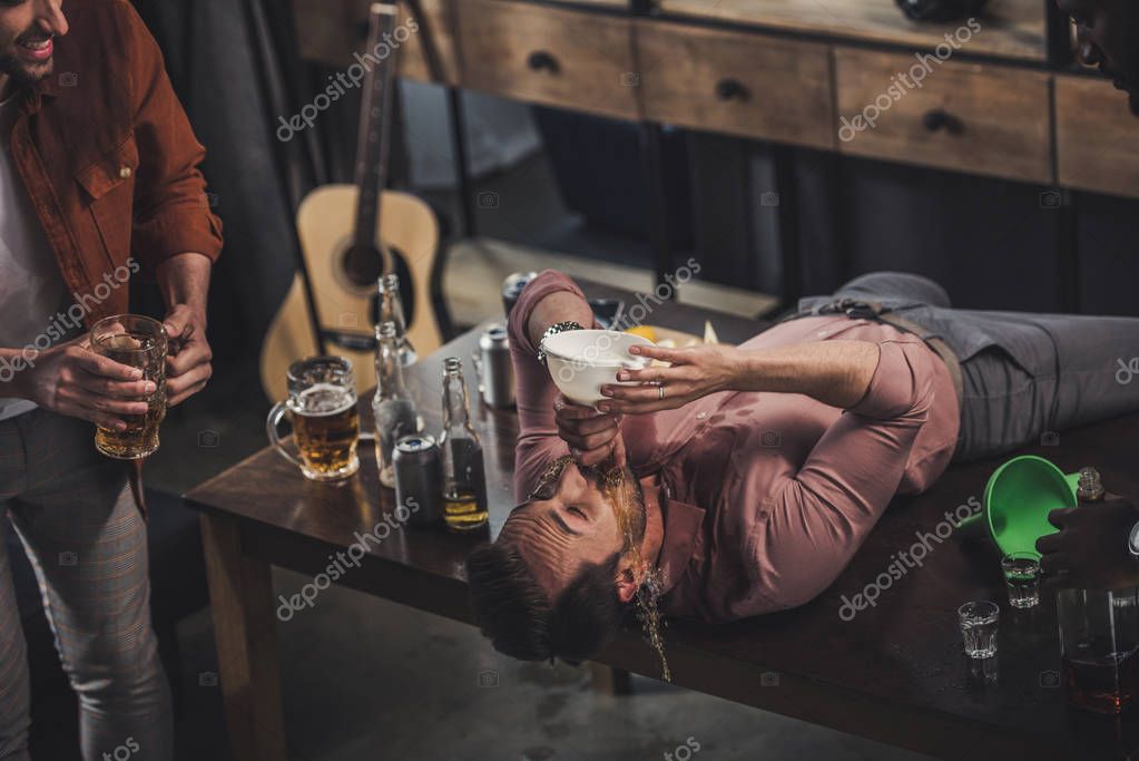 joven acostado en la mesa y bebiendo cerveza del embudo mientras sus ...