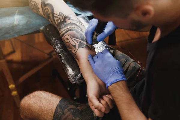 Close up of professional tattooer artist doing picture on hand of man ...