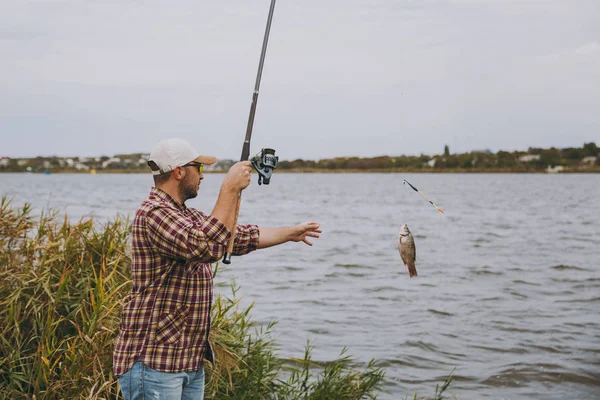 Side view Young unshaven man in checkered shirt, cap, sunglasses pulls ...