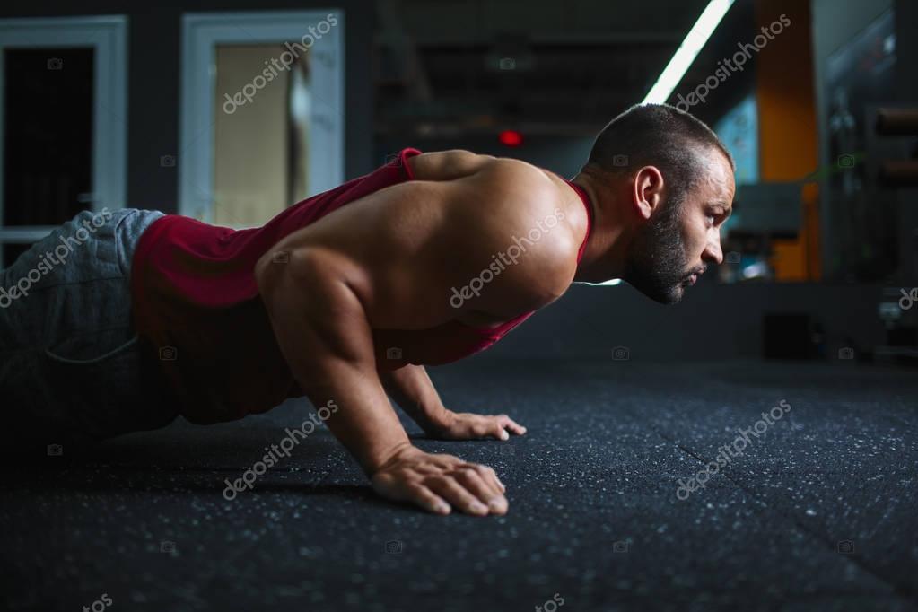 Vista lateral de un joven guapo en ropa deportiva haciendo flexiones en el gimnasio. Hombre ...