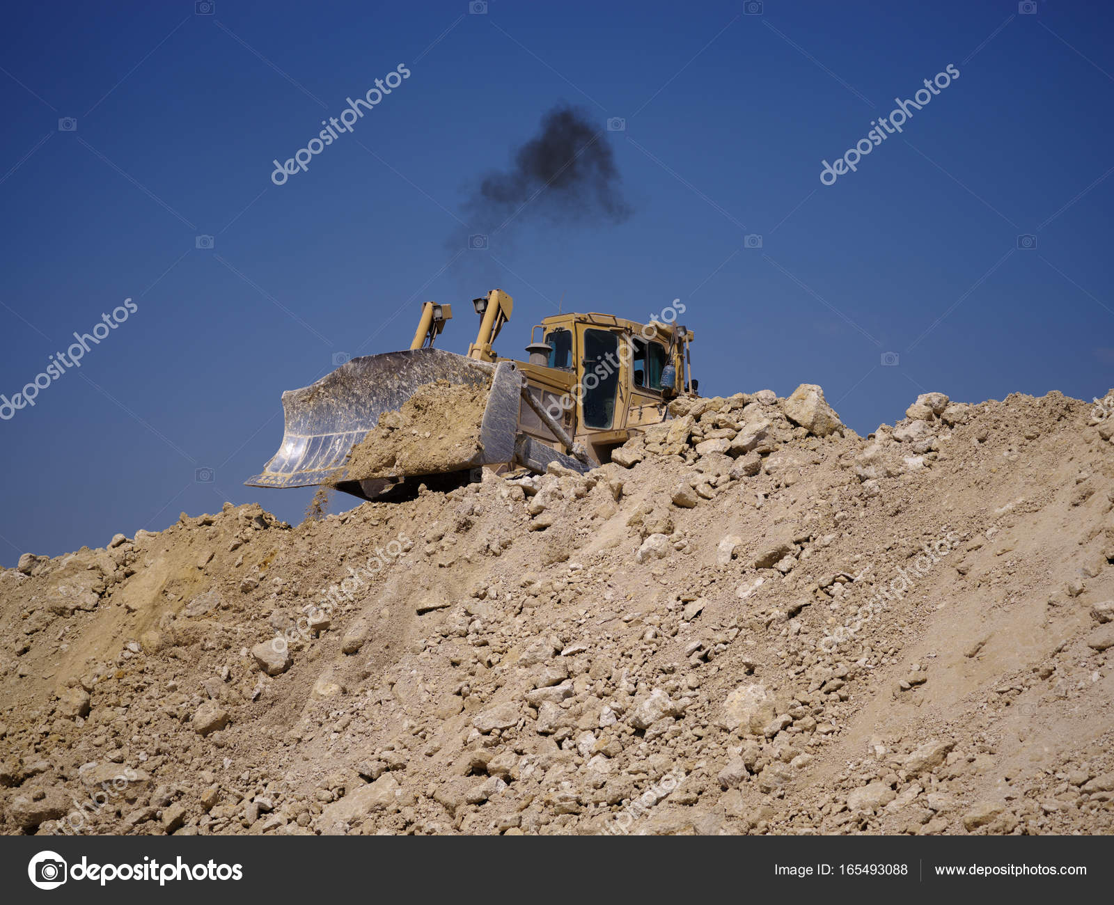 A backhoe loader, a loader backhoe, digger on a heap of sand and stones ...