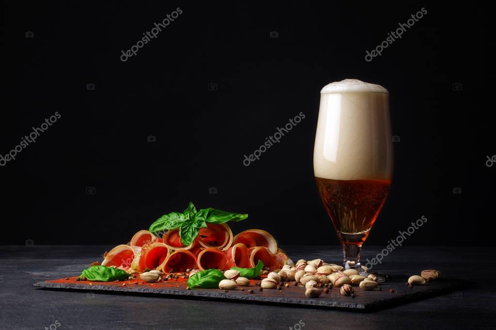 Prosciutto curado con albahaca y una copa de cerveza alcohólica con ...