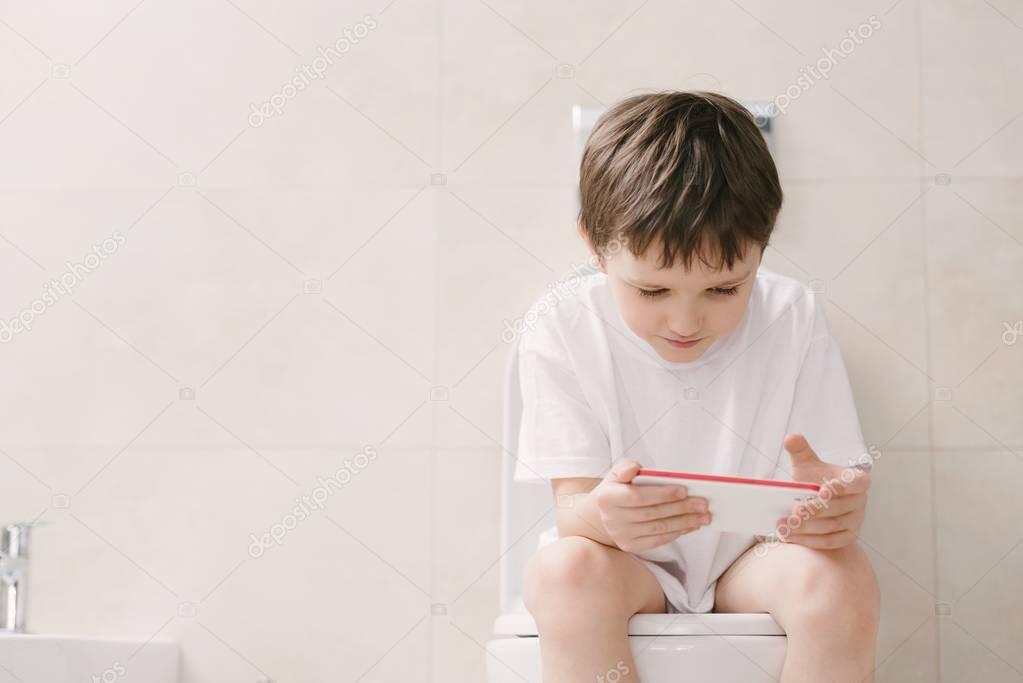Boy playing with smartphone while sitting on toilet. — Stock Photo ...