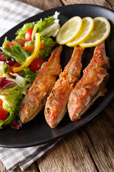 Fried fish red mullet with fresh vegetable salad close-up. verti ...