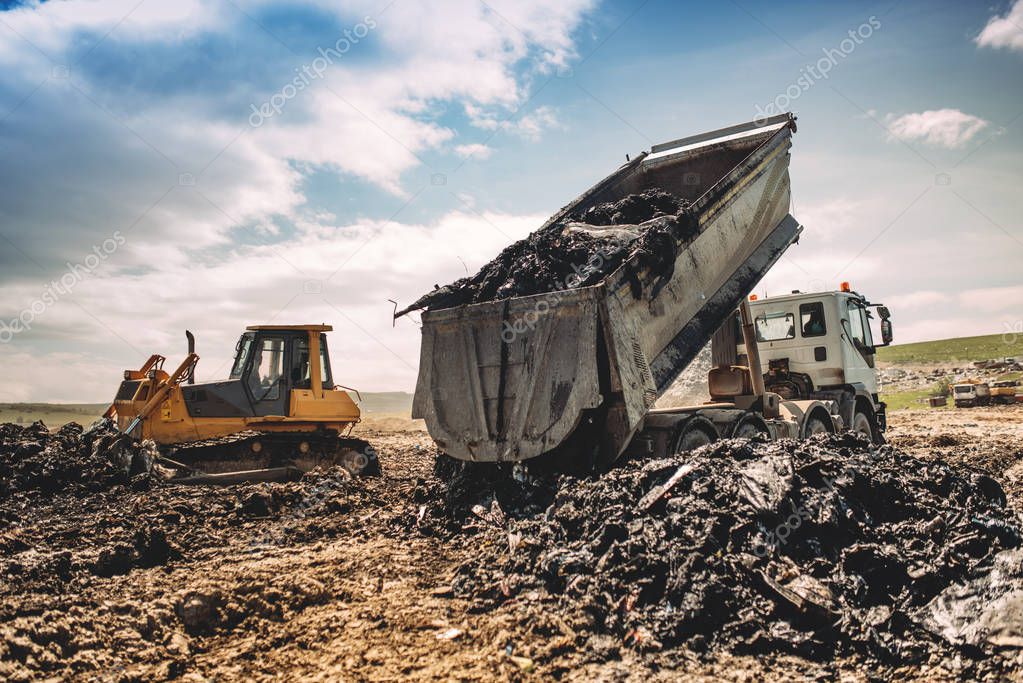 Dumping truck unloading garbage at dumping site. Industrial bulldozer ...