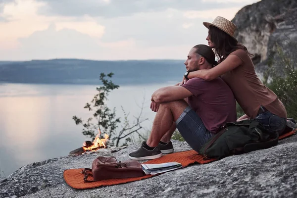 Hugging couple with backpack sitting near the fire on top of mountain ...