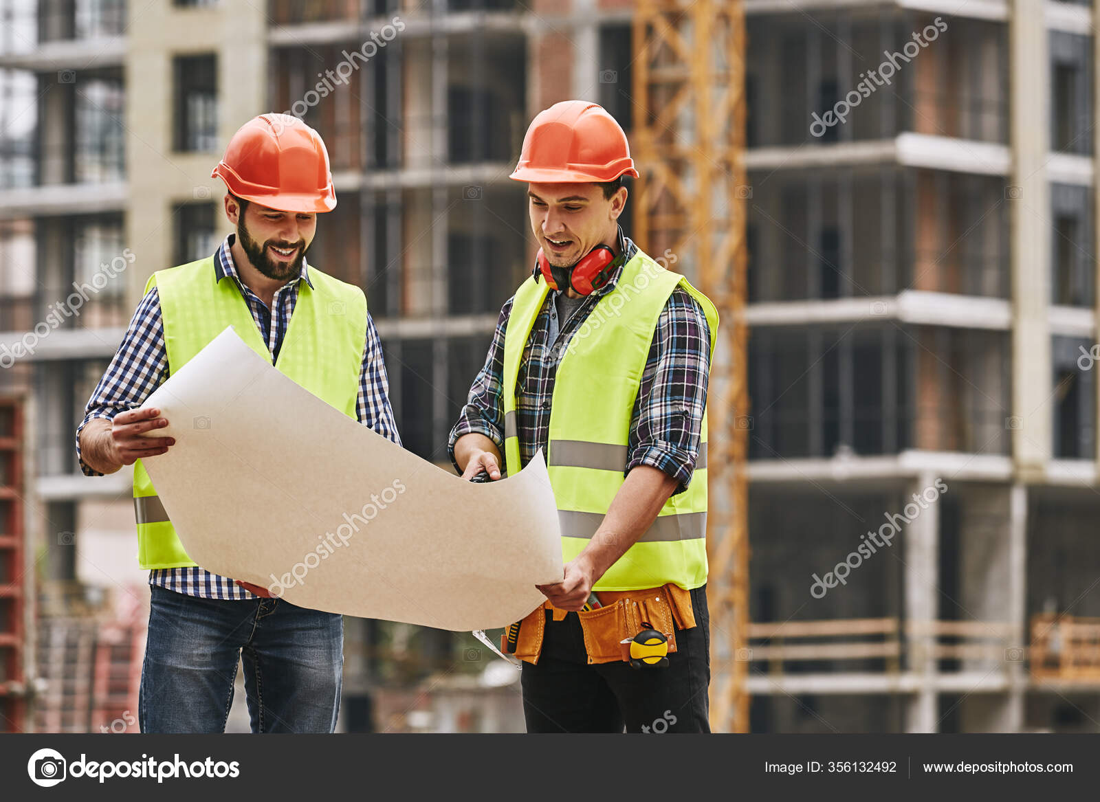 Look here Two young builders in working uniform and helmets are holding ...