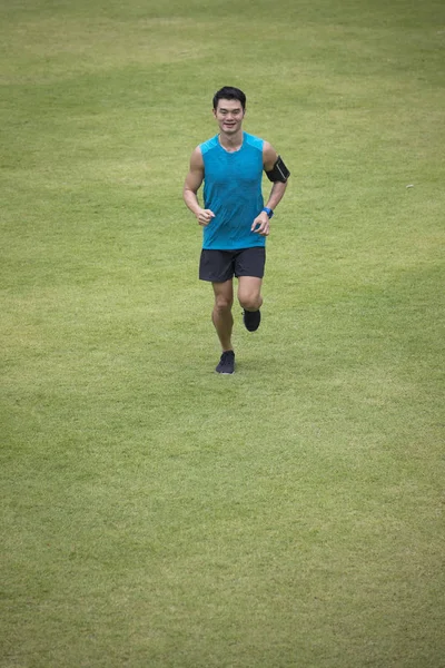 Chinese man jogging across grass field - Stock Image - Everypixel