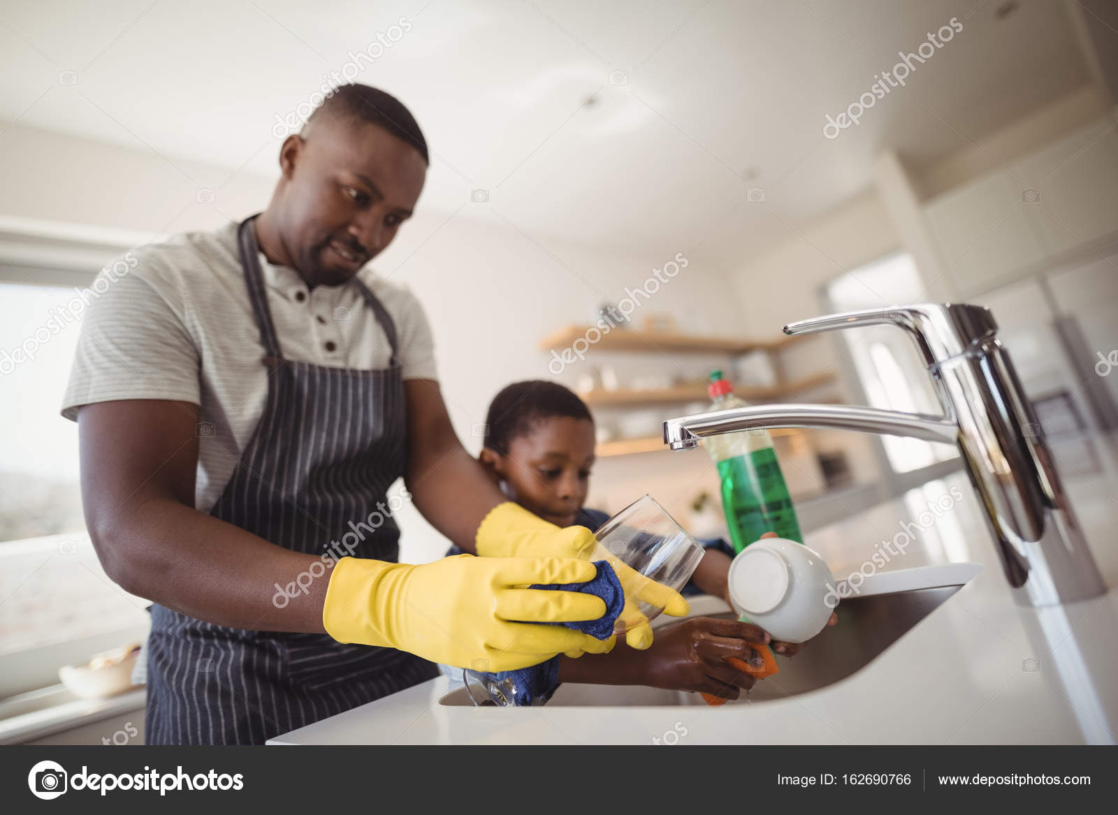 Father and son cleaning utensils in kitchen Stock Photo by ...