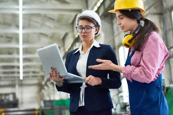 Attractive young technician wearing hardhat and overall and her middle ...