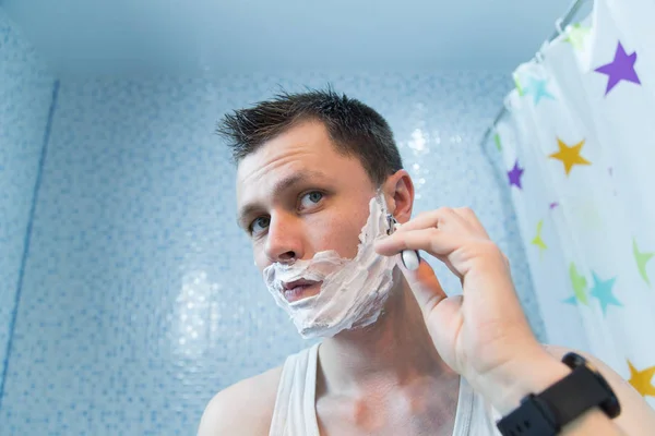 A man shaves his face in the foam with a razor. Guy shaves in front of ...