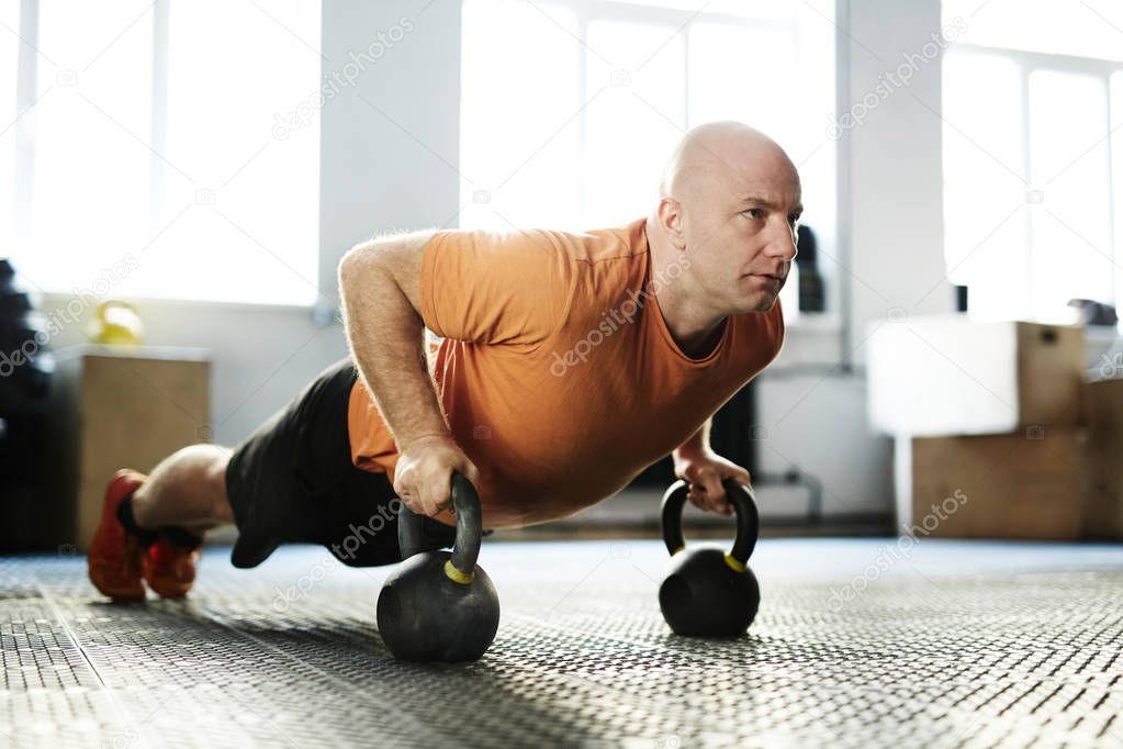 Hombre en forma concentrada haciendo flexiones con pesas contra pared ...