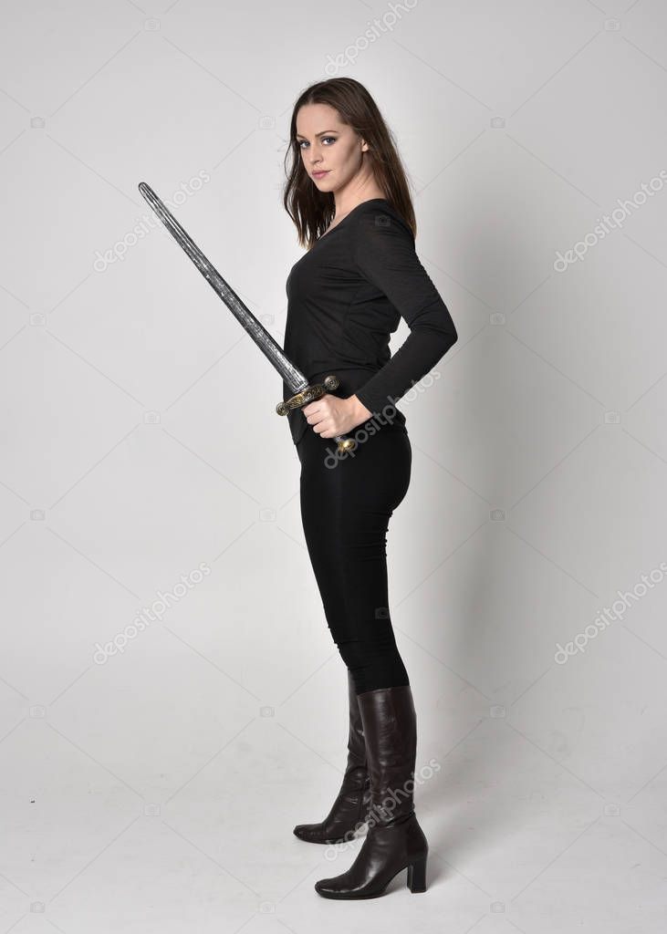 retrato de cuerpo entero de una guapa morena con camisa negra y botas de cuero, sosteniendo una ...