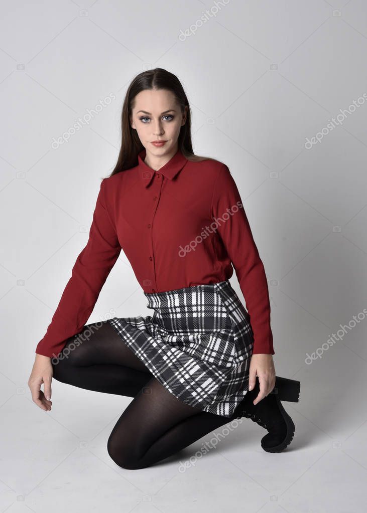 retrato de cuerpo entero de una guapa morena con camisa roja y falda a cuadros con polainas y ...
