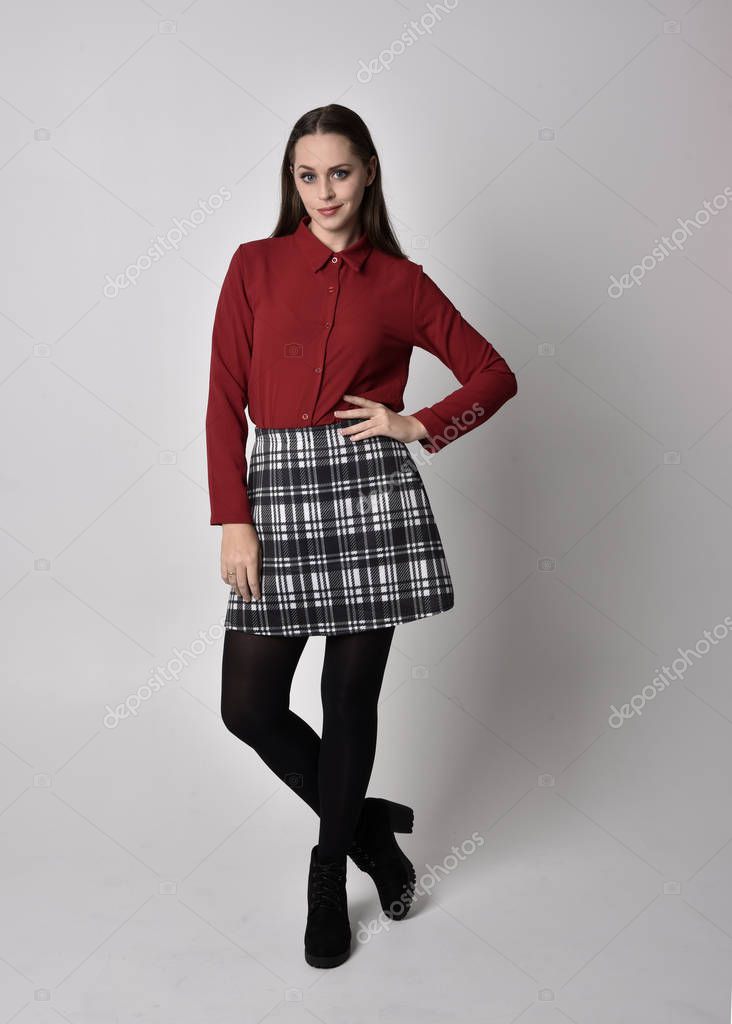 retrato de cuerpo entero de una guapa morena con camisa roja y falda a cuadros con polainas y ...