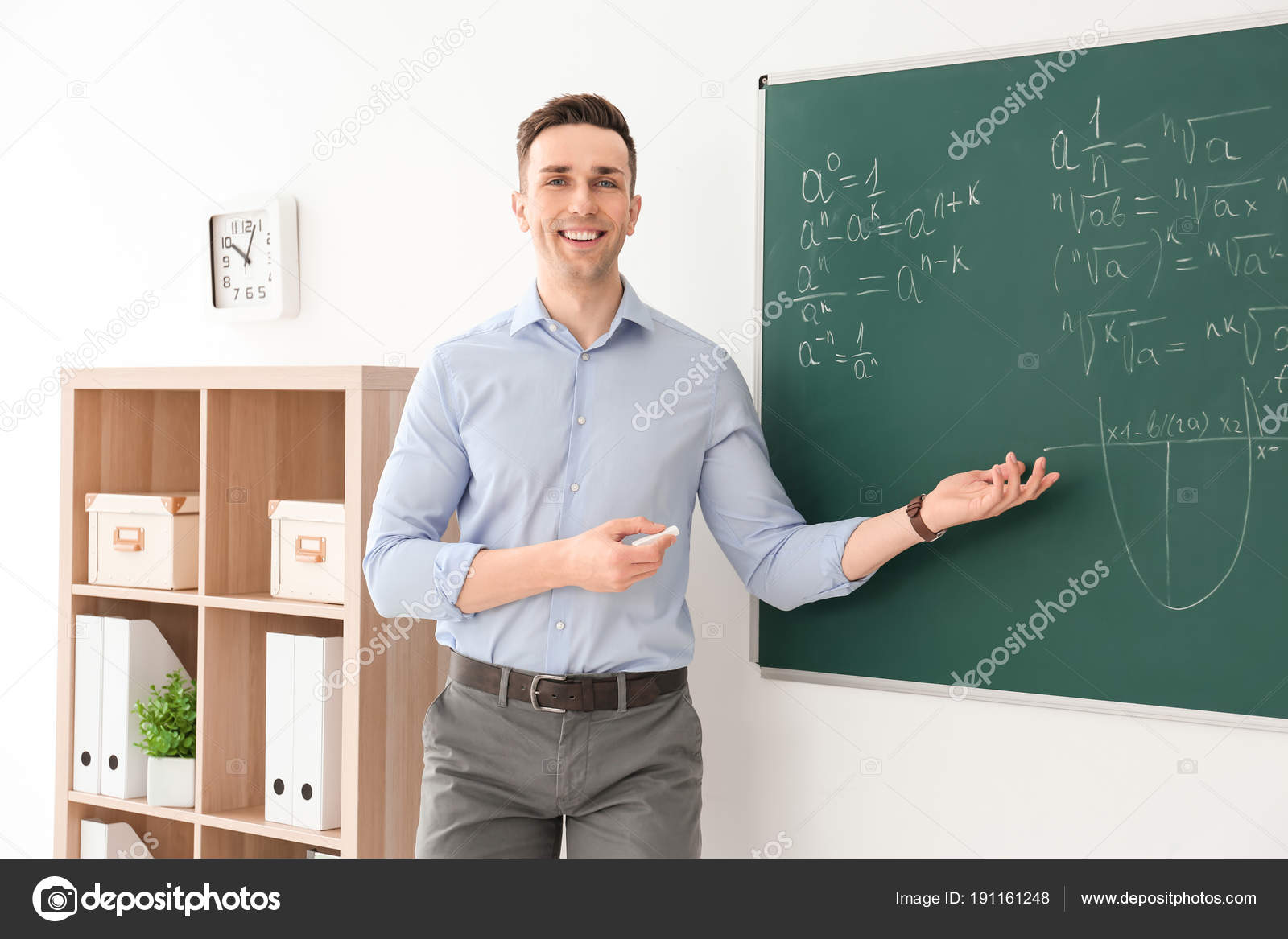 Young male teacher explaining math formulas written on blackboard in ...
