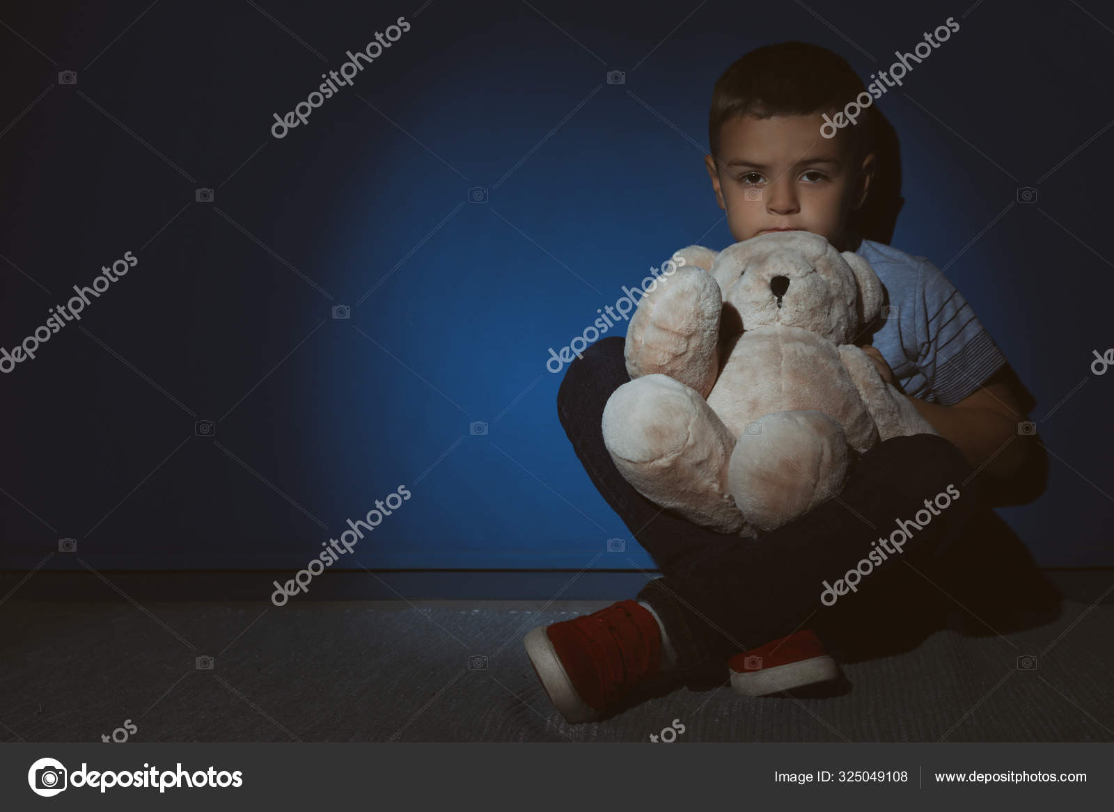 Sad little boy with teddy bear near blue wall, space for text. D ...