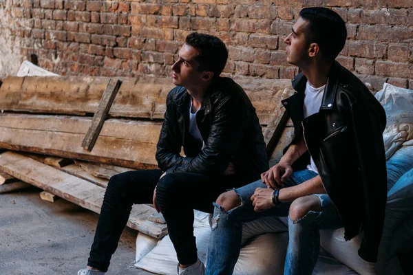 beautiful and attractive guy sit on white bags against a brick wall ...