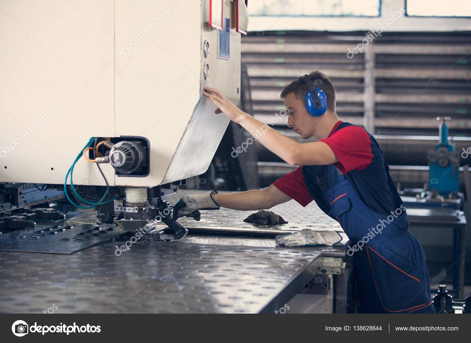 Inside a factory, industrial worker in action on metal press machine ...