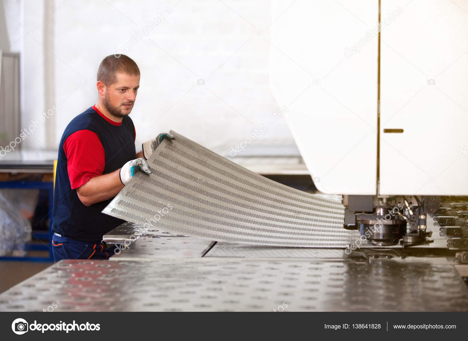 Inside a factory, industrial worker in action on metal press machine ...