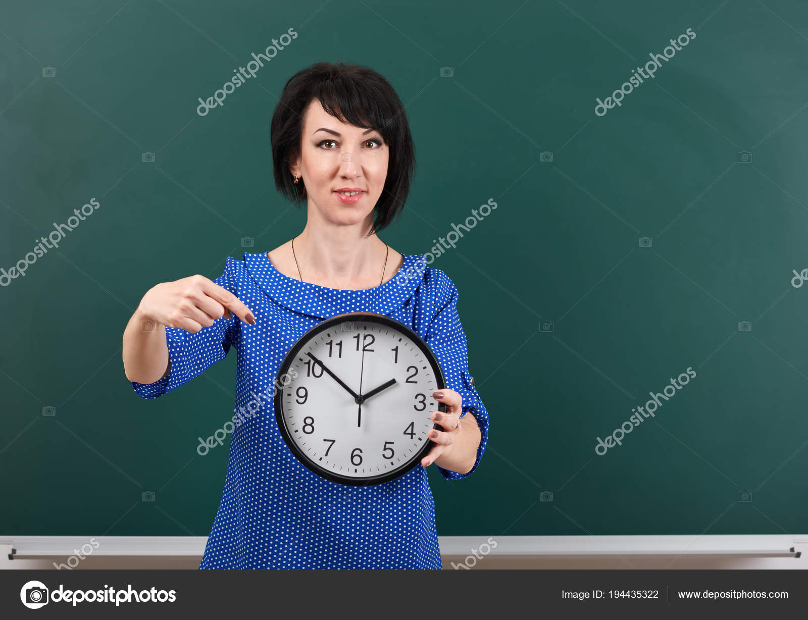 Woman pointing finger at the watch, posing by chalk board, time and ...