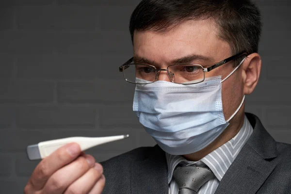 man measures body temperature with a thermometer, checks his health ...