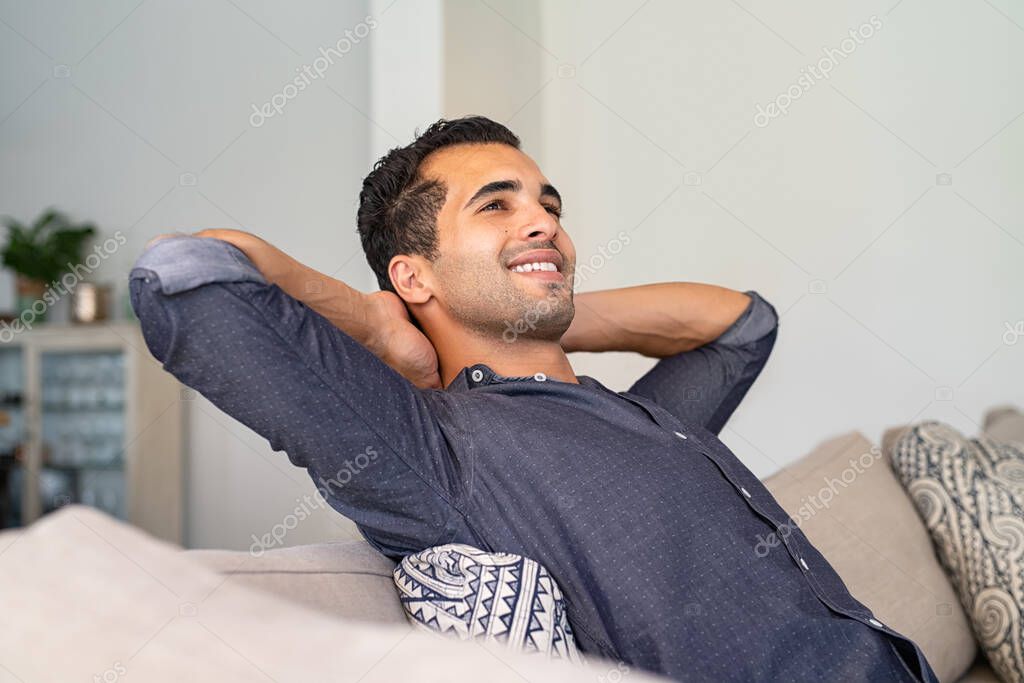Hombre joven indio en casa relajándose y pensando con las manos detrás ...