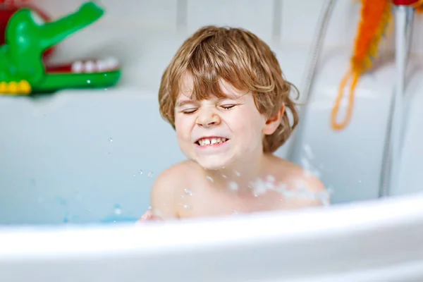 Söt liten barn leker med vatten genom att bada i badkar hemma ...