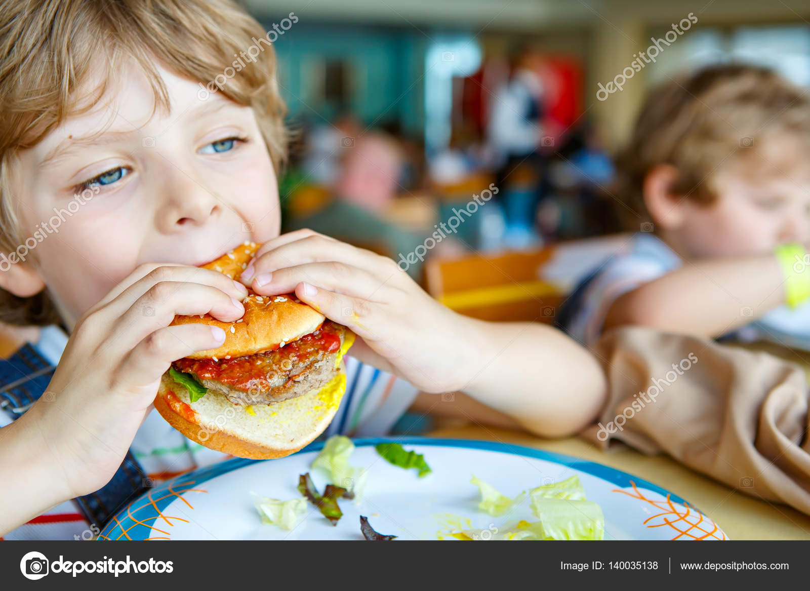 Cute healthy preschool boy eats hamburger sitting in school canteen ...