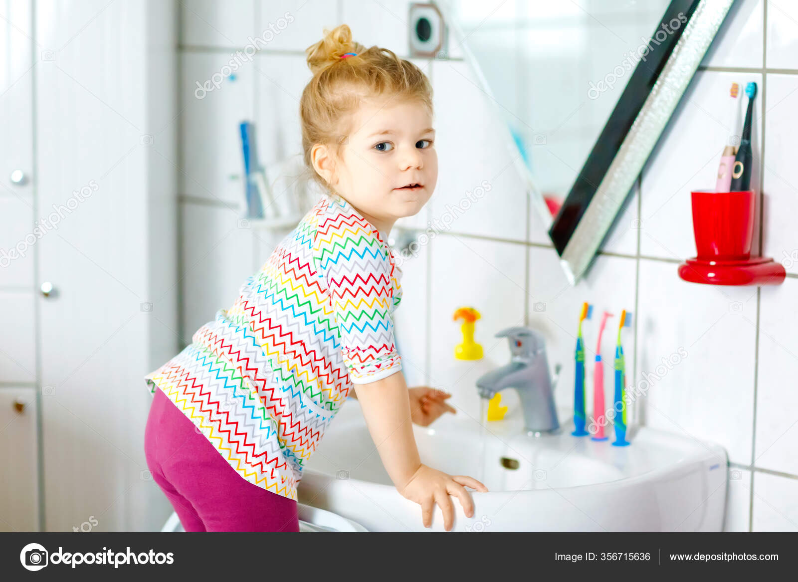 Cute little toddler girl washing hands with soap and water in bathroom ...