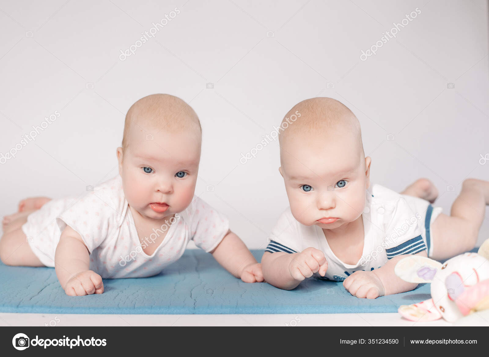 Two beautiful little babies lies on a bed together and looks to the ...