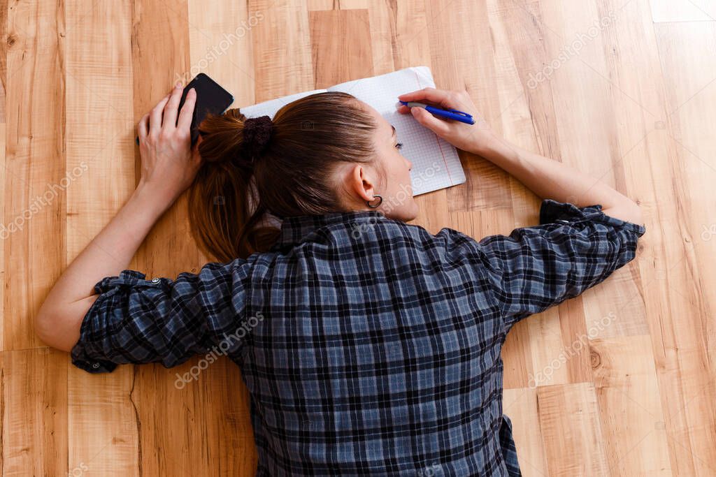 mujer cansada se encuentra en el suelo con un cuaderno y un trabajo pen ...