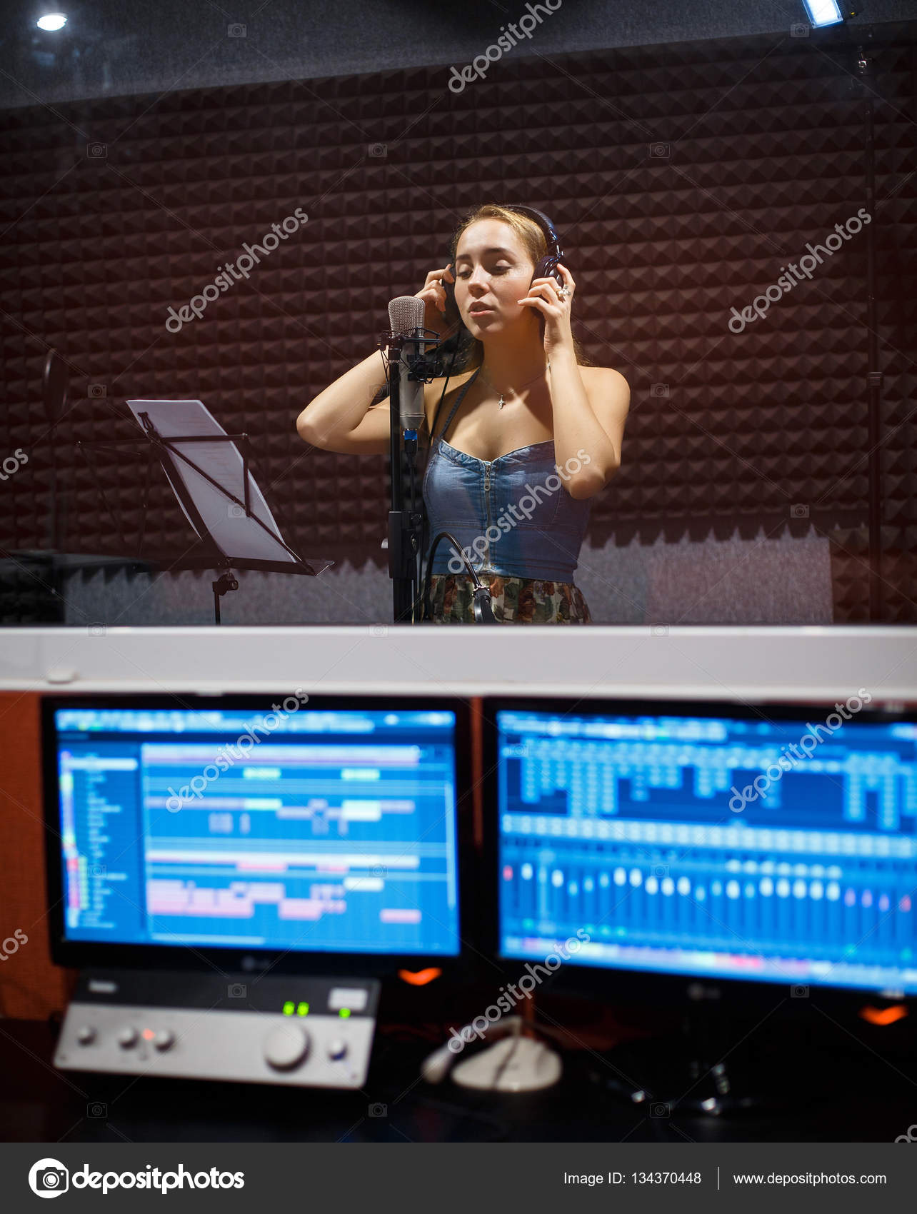 Girl singing in professional studio with mic, headphones and computers ...