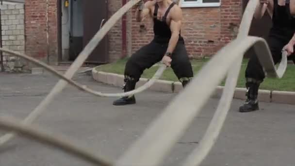 Two young muscular men train and do exercises with a rope and a ...