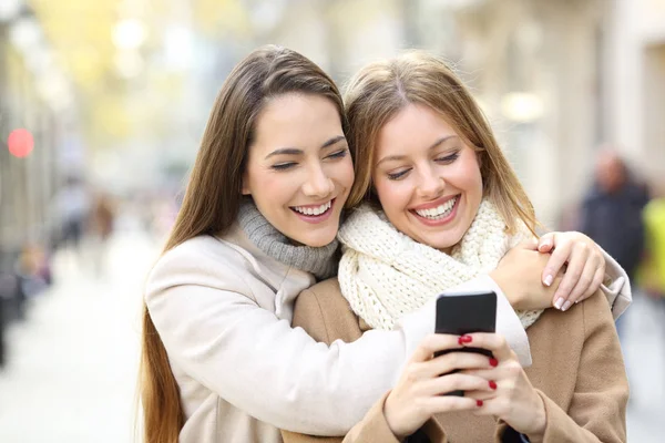 Two friends watching smart phone content in winter - Stock Image ...