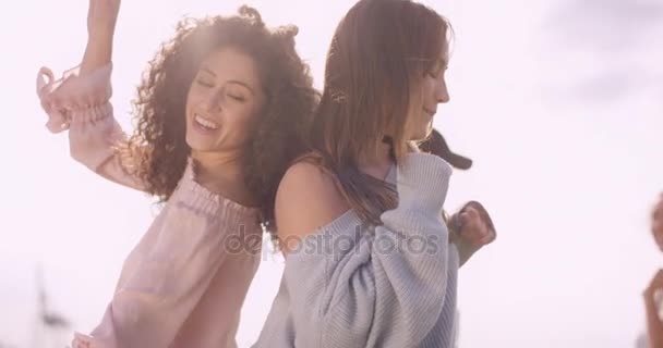 Two young women dancing back to back, with glasses in their hands and ...