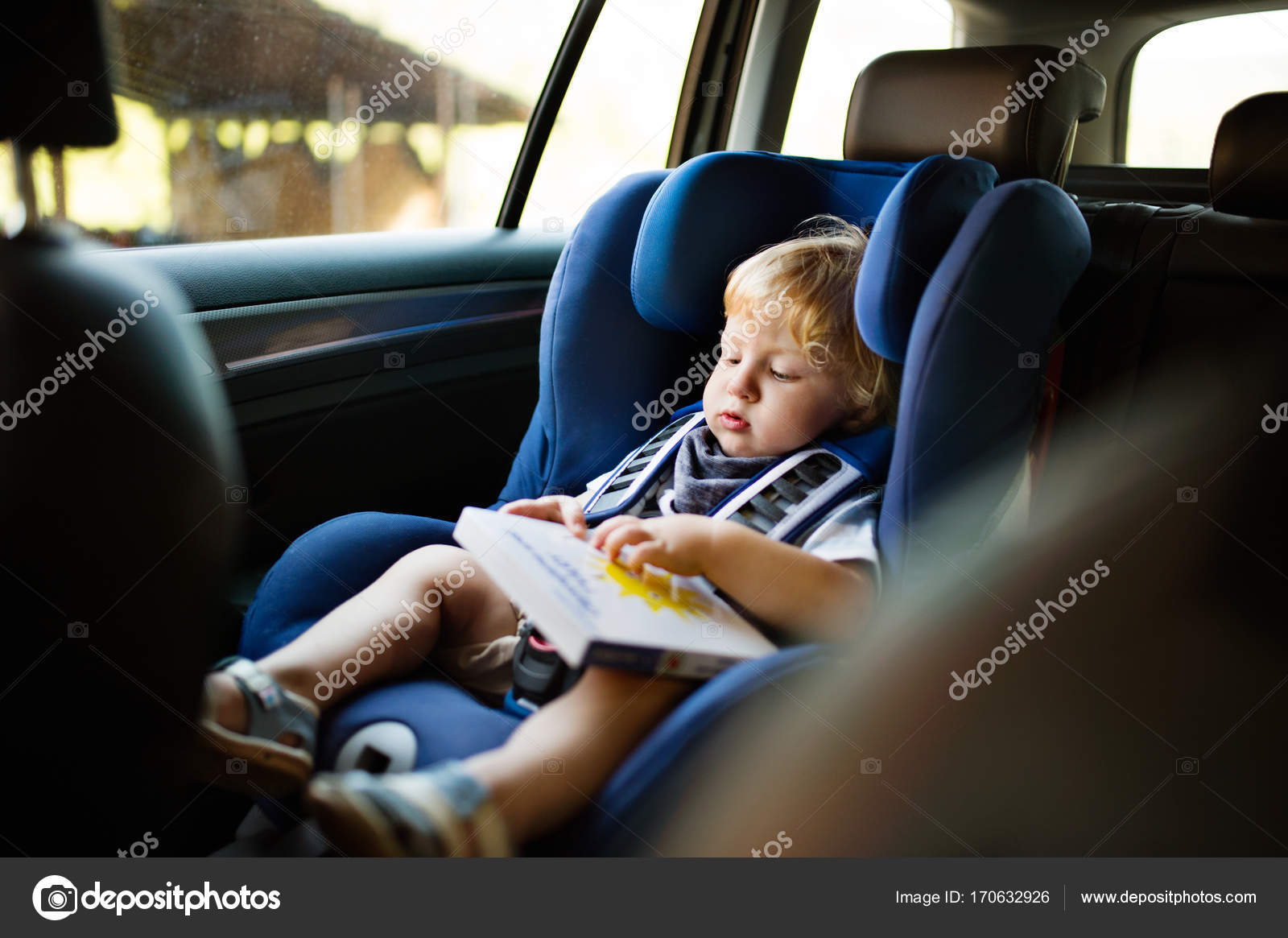 Little boy sitting in the car seat in the car, holding a book. Stock ...
